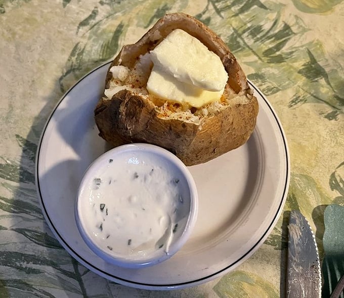 A baked potato arrives like a fluffy cloud of comfort – split open, steaming, and ready for its sour cream crown.