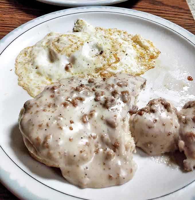 Biscuits and gravy that would make a Southern grandmother weep with joy, accompanied by a perfectly cooked sunny-side-up egg.