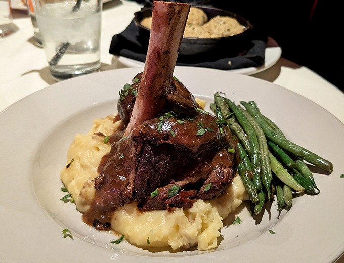 The lamb shank arrives like meat architecture – a tower of tender goodness that surrenders to your fork with barely a nudge.