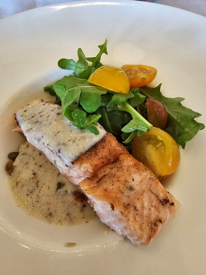 Perfectly seared salmon rests on a bed of lentils, accompanied by fresh greens and heirloom tomatoes &ndash; simple elegance on a plate.