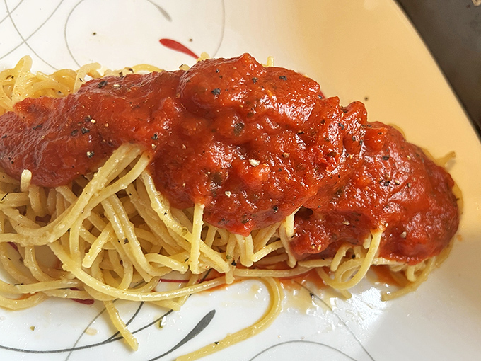 Steam rises from this generous serving of spaghetti, its sauce glistening under the lights like a tomato-based lullaby for your appetite.