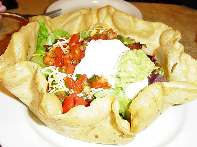 The taco salad arrives in its edible fortress, a crispy tortilla bowl protecting the fresh treasures within like a delicious suit of armor.
