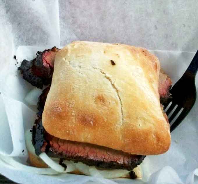 This crusty ciabatta roll barely contains the generous portion of pink-ringed brisket, a handheld masterpiece of smoke and beef.