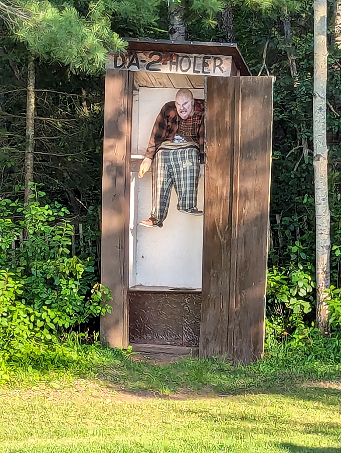 This rustic outhouse display features a mannequin in plaid pants, capturing the essence of northwoods bathroom humor.