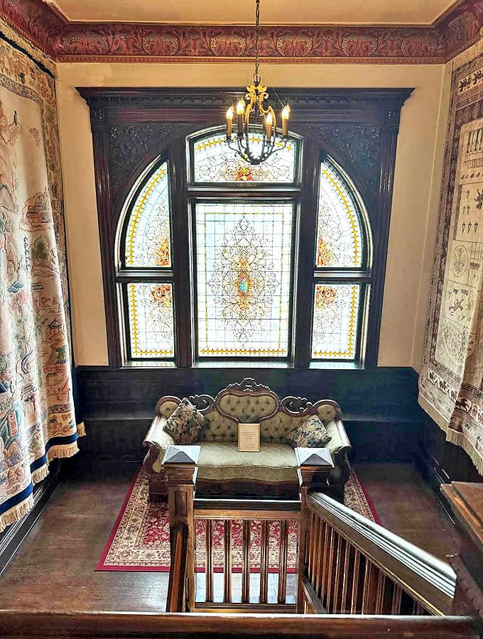 Landing Area: Sunlight streams through magnificent stained glass, creating a kaleidoscope of colors on antique furnishings in this peaceful reading nook.