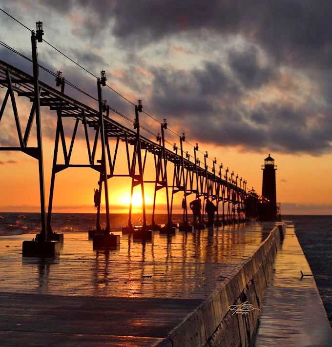 Silhouettes dance along the pier at sunset, with the lighthouse creating a dramatic backdrop for end-of-day strolls.