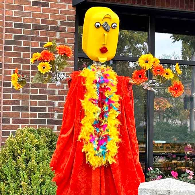 Draped in vibrant red with a sunny yellow face, this floral-adorned figure stands like a carnival barker welcoming all to the show.