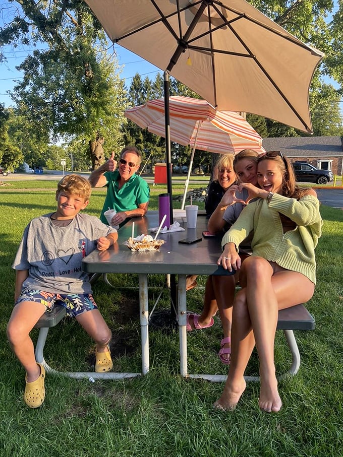 Families gathering at picnic tables under summer skies, creating memories that taste like root beer and sound like laughter.