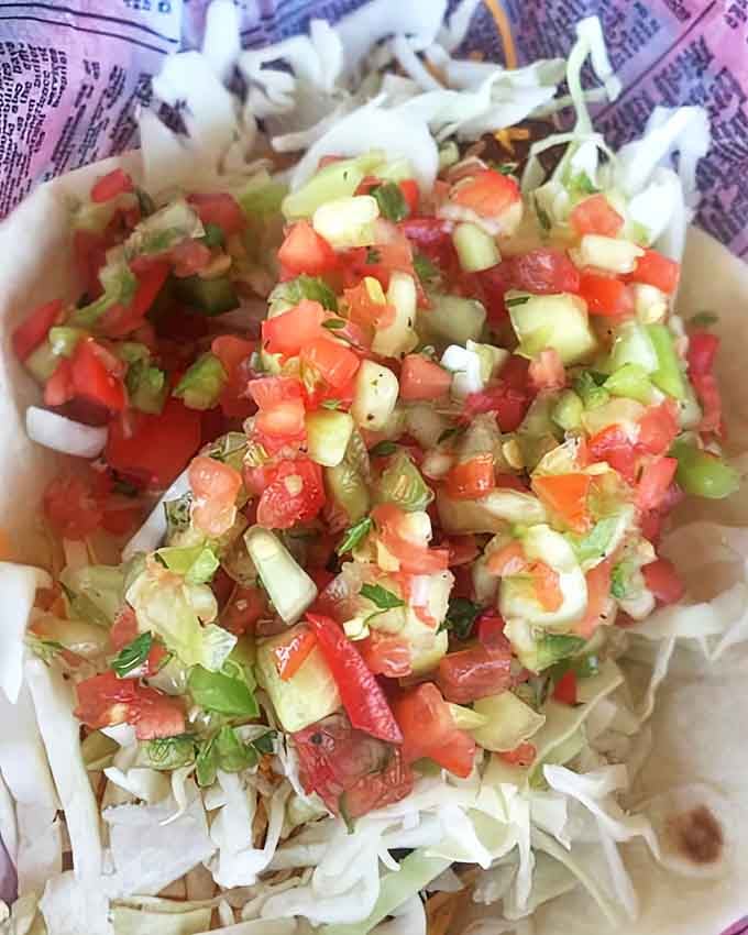 A colorful fiesta of fresh vegetables dancing atop delicate fish, creating a handheld masterpiece that brings together the best of lake and garden.