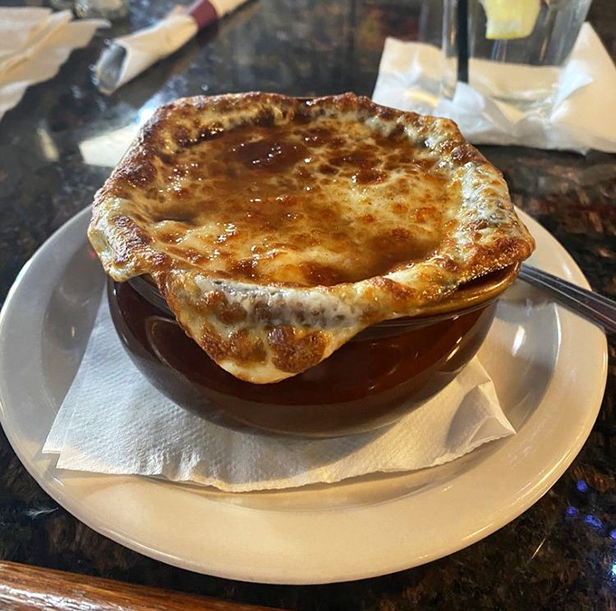 French onion soup arrives with a crown of melted cheese that stretches dramatically, revealing a rich, deeply flavored broth beneath.