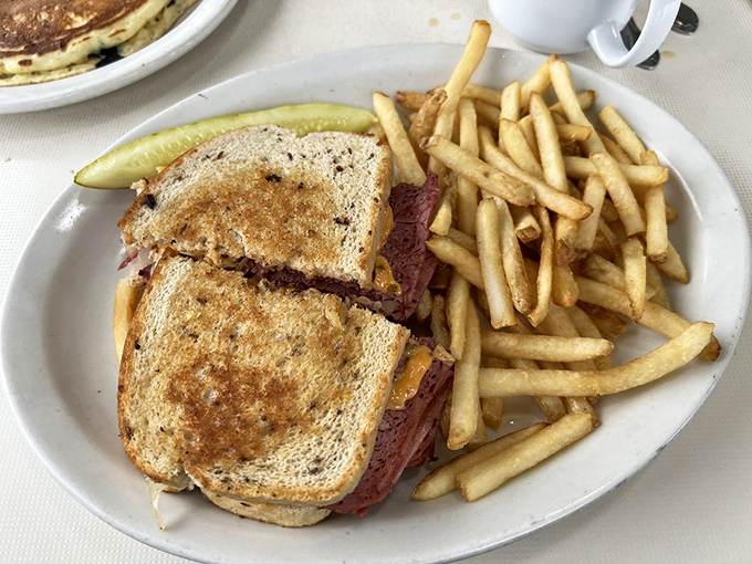 Reuben: A towering testament to sandwich engineering &ndash; tender corned beef, tangy sauerkraut, and melted Swiss on grilled rye with crispy fries.