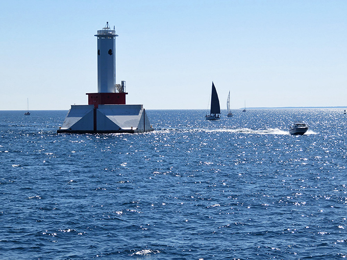 Sailboats glide past the modern light tower, creating a timeless Michigan tableau that belongs on every Great Lakes vacation bucket list.