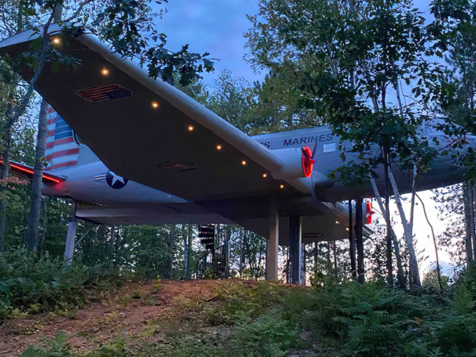Evening transforms the aircraft with subtle red lighting on the propellers, creating a magical forest dwelling.