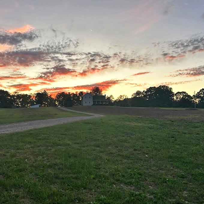 As day surrenders to dusk, the farmhouse silhouette stands sentinel over fields of gold, framed by Michigan's dramatic summer skies.