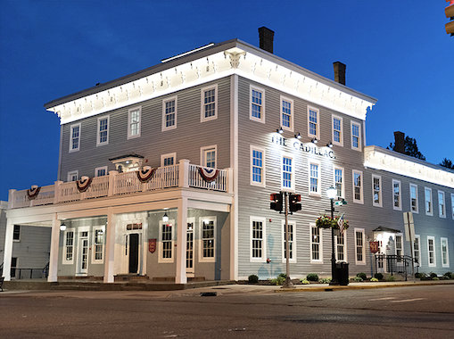 The Cadillac House stands proudly illuminated against the evening sky, its historic fa&ccedil;ade promising modern comforts with a side of yesteryear charm.