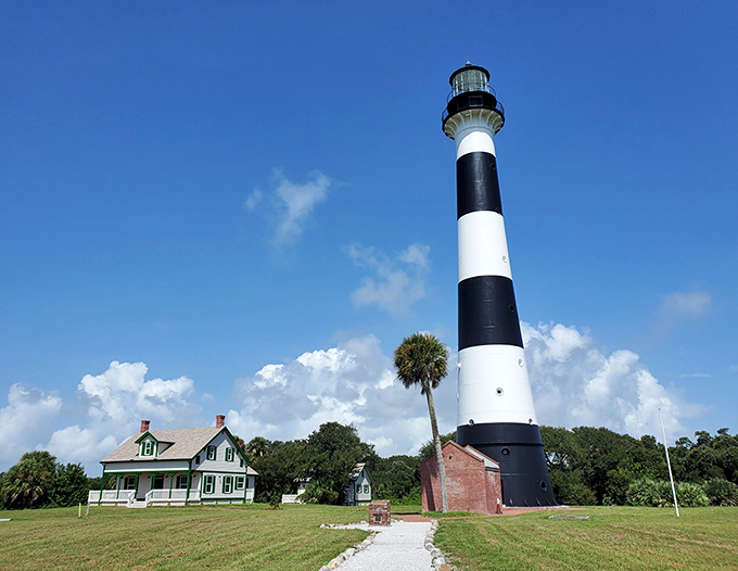 The iconic black and white stripes of Cape Canaveral Lighthouse stand tall against Florida's blue sky, a maritime sentinel with a space-age backdrop.