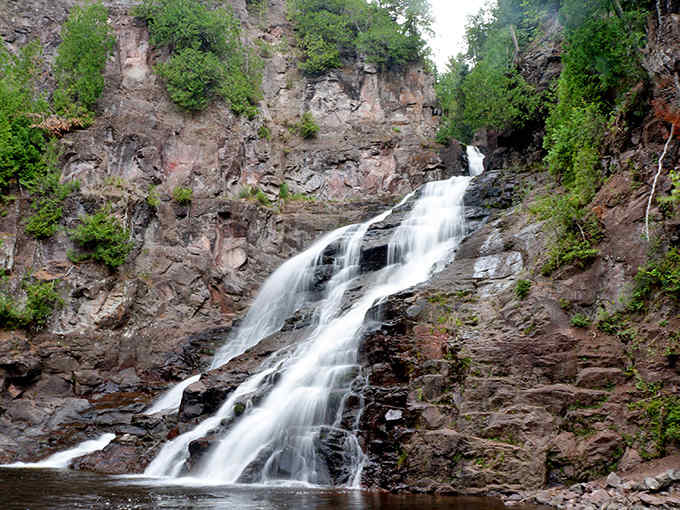 Caribou Falls cascades dramatically down ancient volcanic rock, creating a misty veil that seems to dance in the sunlight.
