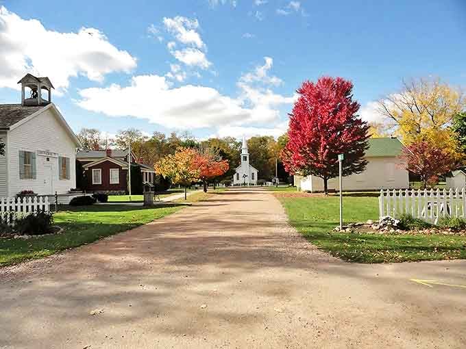 A dirt path winds through Corunna Historical Village, where white picket fences and autumn-painted trees create Michigan's perfect historical postcard.
