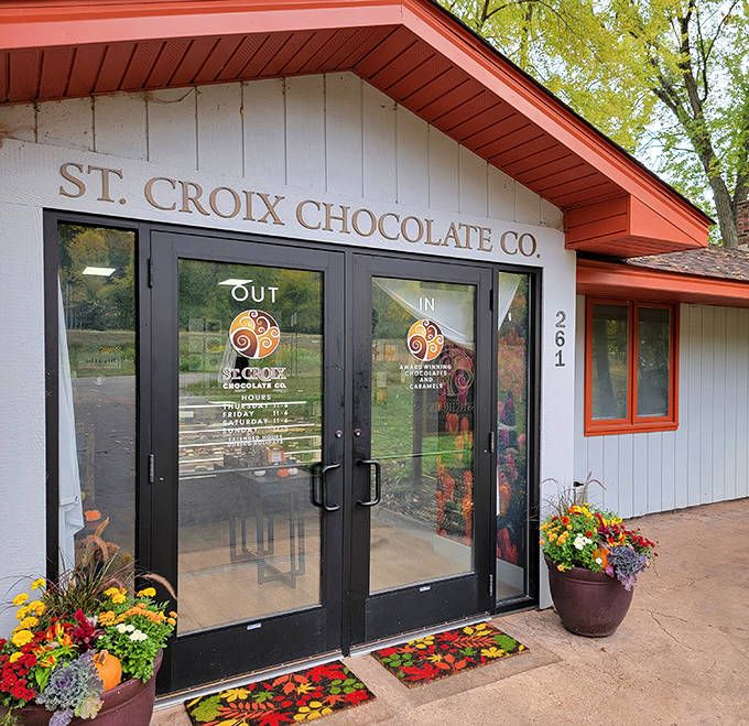 The charming exterior of St. Croix Chocolate Co. welcomes chocolate lovers with its distinctive orange-trimmed roof and seasonal flower displays.