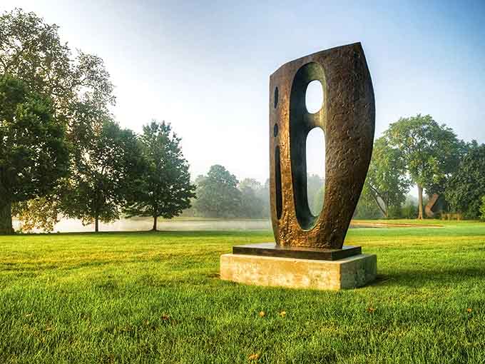 A bronze sentinel stands guard in morning mist, its curved form creating a perfect window to frame the landscape beyond.
