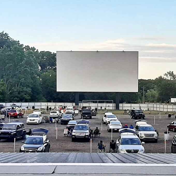 The massive white screen stands ready against the twilight sky, a blank canvas awaiting cinematic magic as cars find their perfect viewing spots.