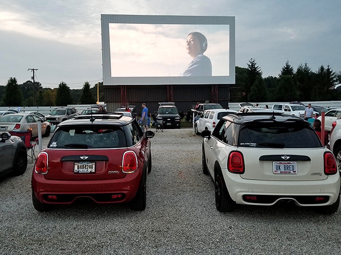Cars line up at dusk, headlights dimming as the massive screen awakens with cinematic magic at Midway Drive-In Theater.