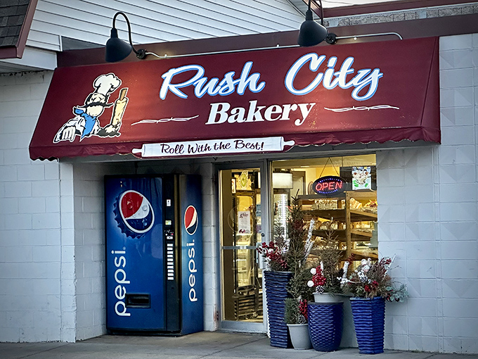 The iconic red awning of Rush City Bakery welcomes visitors with its charming "Roll With the Best!" slogan and vintage baker character.