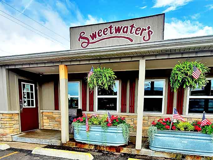 Sweetwater's welcoming exterior beckons with its charming red signage and flower-filled galvanized planters &ndash; a humble facade hiding donut greatness within.