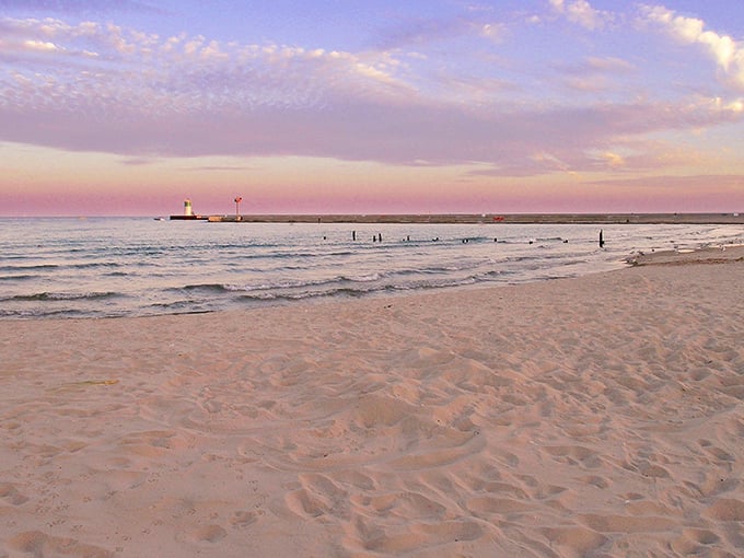 Sunset paints Waukegan Beach in cotton candy hues, the lighthouse standing sentinel as day bids farewell to Lake Michigan's shimmering waters.