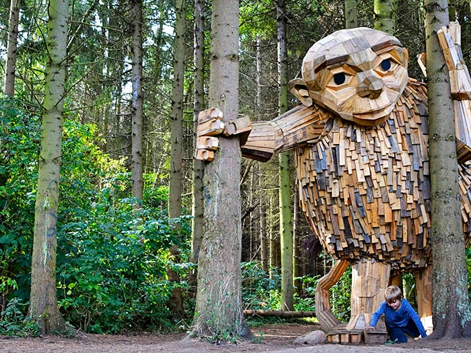 A gentle wooden giant peeks through the forest, his shingle-covered face a testament to recycled artistry at its finest.