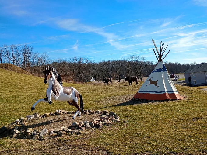 A painted horse statue rears dramatically beside a teepee, creating a scene straight from a vintage Western postcard.