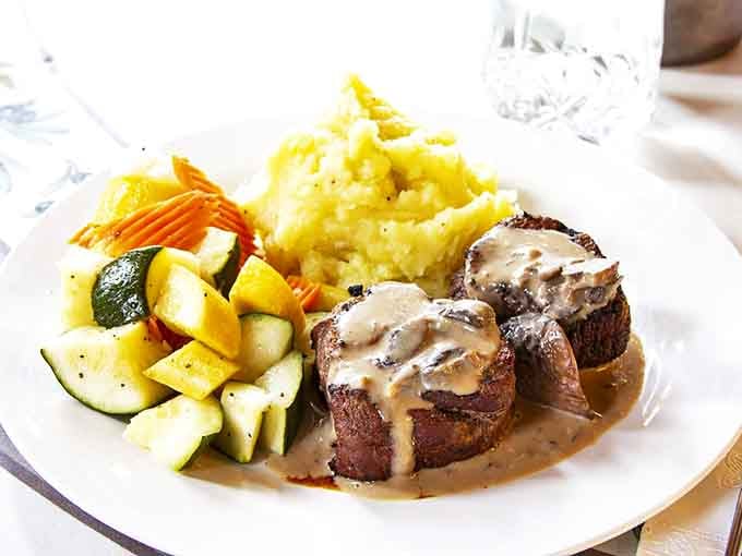 Beef medallions bathed in velvety mushroom gravy, accompanied by cloud-like mashed potatoes and seasonal vegetables &ndash; comfort food at its finest.