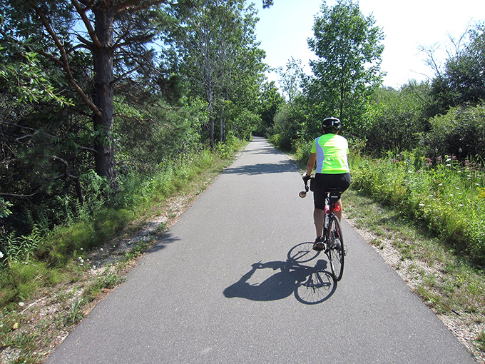 Dappled sunlight creates a natural light show on this forested section, where cyclists glide through cool shadows on hot summer days.
