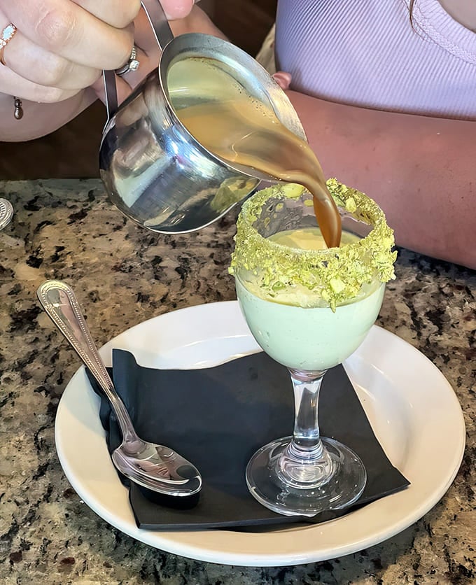 Pistachio cream meets espresso in this theatrical presentation where hot coffee pours over green-rimmed sweetness, creating Instagram gold and flavor heaven simultaneously.