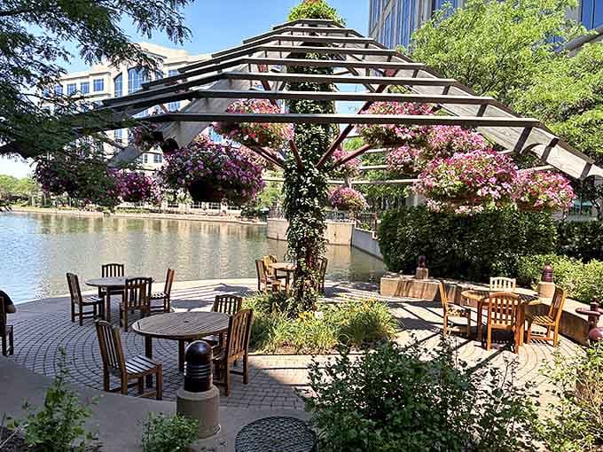The lakeside dining area offers al fresco ambiance under a wooden pergola, where hanging baskets of vibrant flowers create a ceiling of living color.