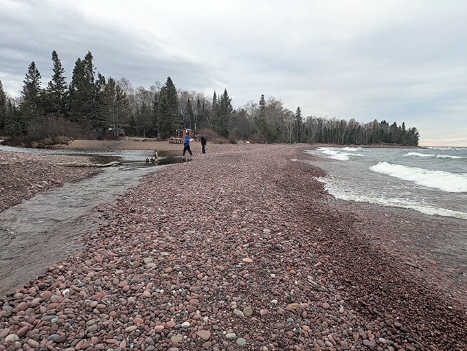 Fellow adventurers stroll along the stone-covered beach, dwarfed by the vastness of Lake Superior stretching to the horizon.