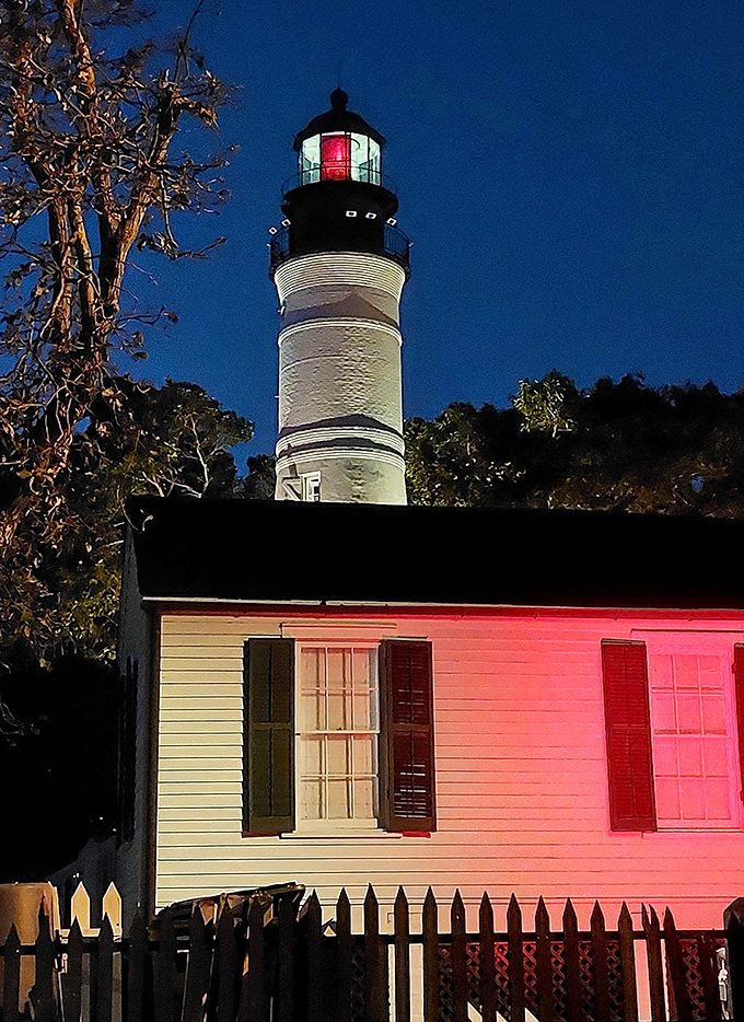 As night falls, the lighthouse transforms into a glowing sentinel, its red and white lights cutting through the darkness.