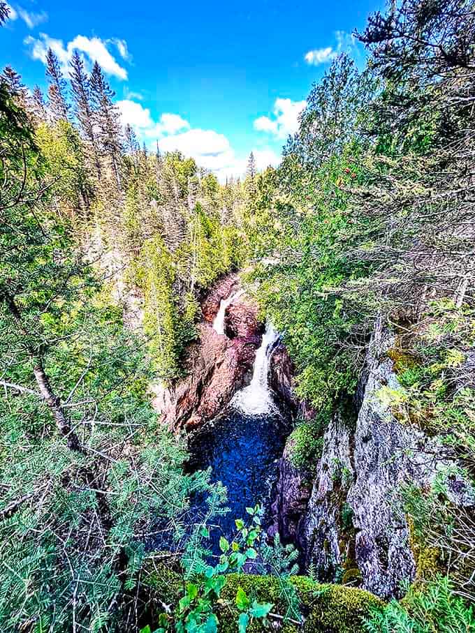 A breathtaking aerial perspective reveals the waterfall's dramatic plunge into its mysterious pothole, surrounded by Minnesota's northern forest.