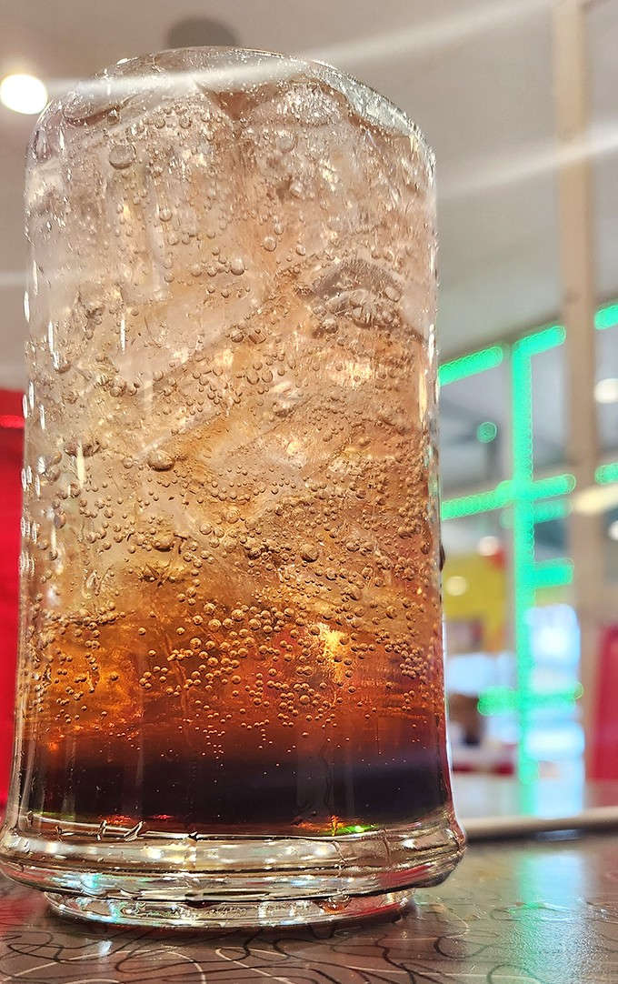 That ice-cold soda in a classic glass – bubbles rising like tiny time machines, each sip fizzing with nostalgia and pure refreshment.