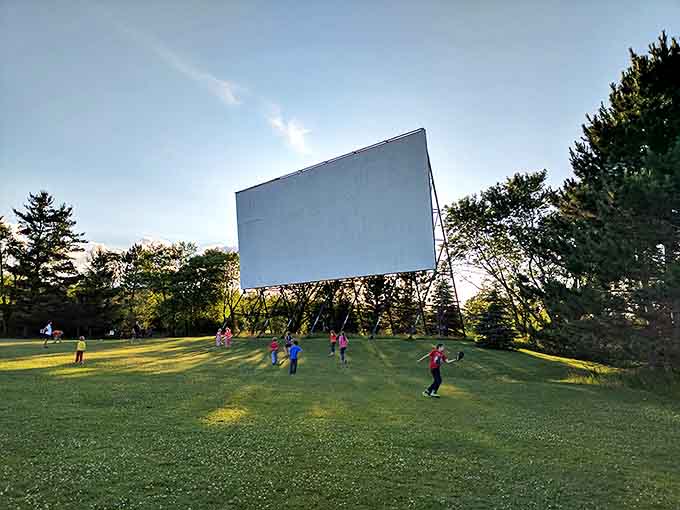 The grassy area beneath the screen transforms into an impromptu playground, where tomorrow's drive-in regulars create pre-show memories.
