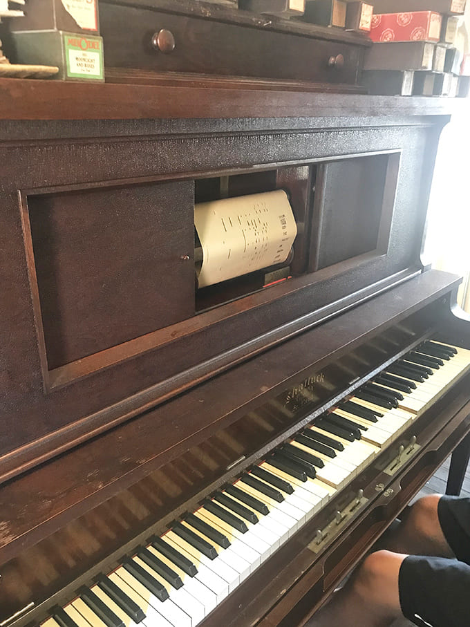 The player piano stands ready, its yellowed music roll still in place – waiting for someone to pump the pedals and fill the store with melody.