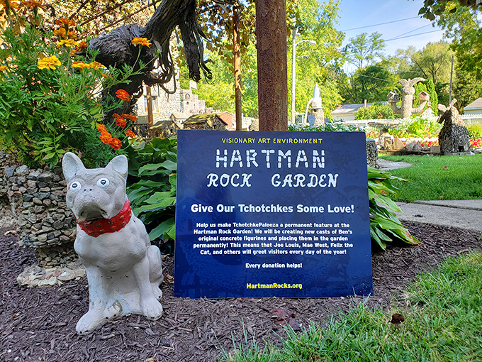 A playful dog statue guards a sign requesting donations to preserve the "tchotchkes" &ndash; the garden's charming collection of figurines and decorations.