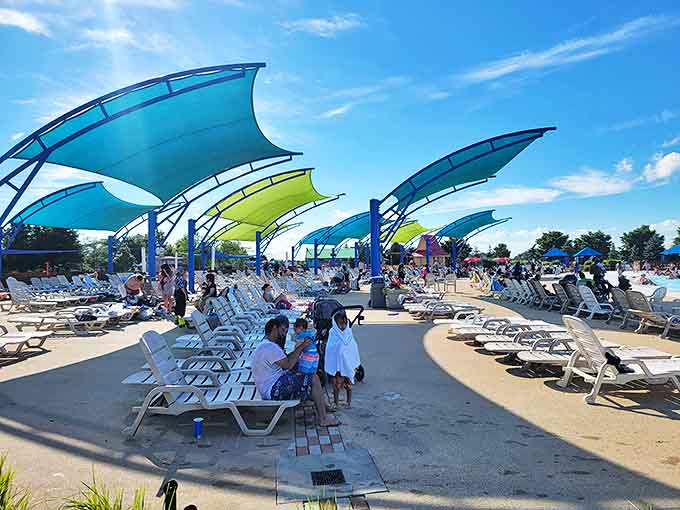 Lounge chairs await weary swimmers under colorful shade sails &ndash; strategic rest stops for parents pretending they're "just taking a quick break."