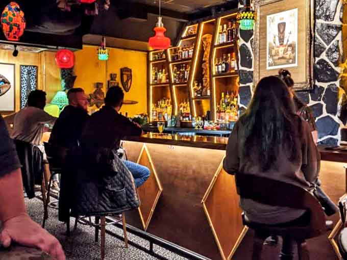 Patrons perch at the dramatically lit bar where mixologists craft elaborate tropical concoctions with theatrical flair and precision.