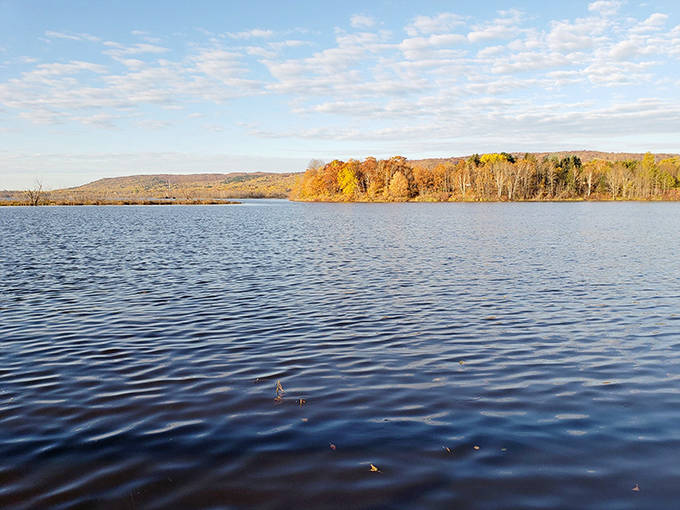 Calm waters mirror the autumn hillside, doubling nature's splendor as seen from strategic viewpoints along the railroad journey.