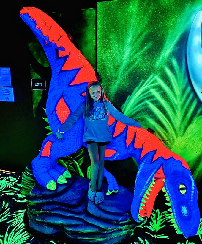 A young visitor stands beneath a towering dinosaur, experiencing that perfect blend of wonder and "is this thing going to eat me?"