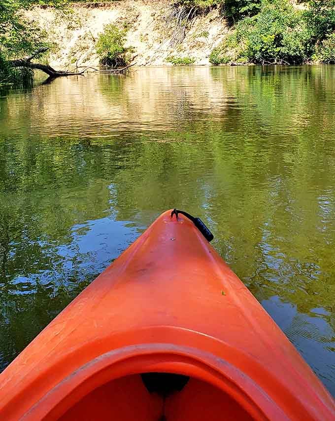 The bow of a bright orange kayak cuts through golden waters, a first-person perspective of adventure waiting around each bend.