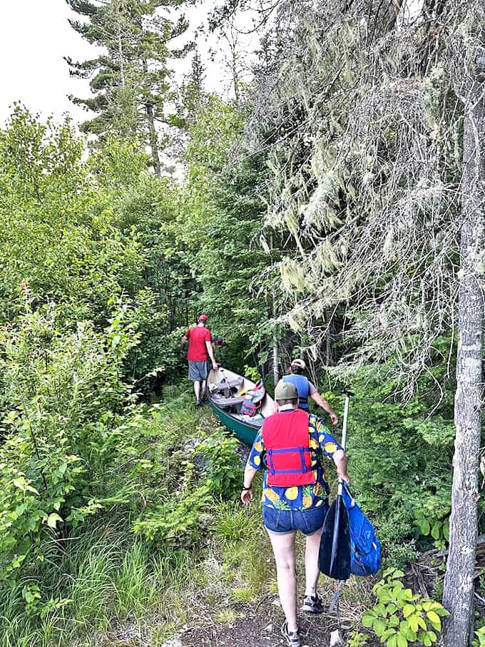 The portage tradition continues as hikers carry their canoe through a forest trail, connecting waterways the way explorers have for centuries.