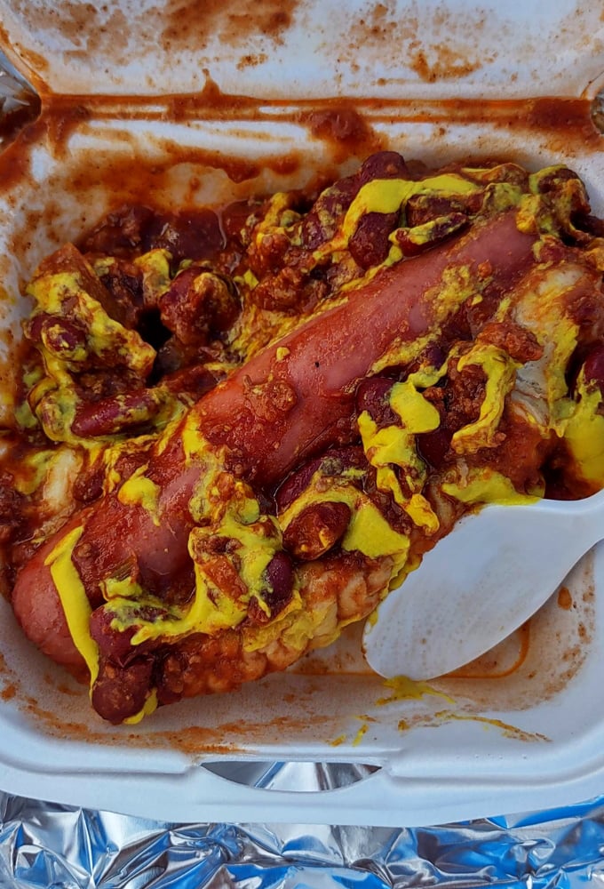 A hot dog transformed into an event &ndash; smothered in chili and mustard, it's a fork-required feast that defies traditional hot dog etiquette.