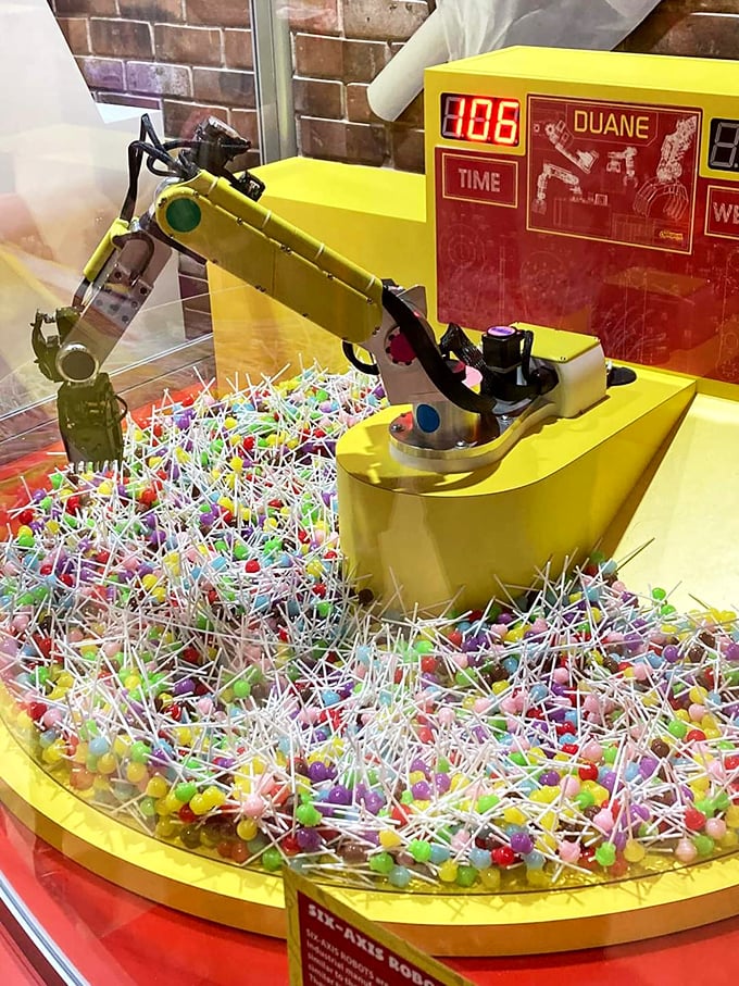 The robotic candy-picking arm hovers over a sea of lollipops, demonstrating how modern technology meets traditional candy-making in this sweet factory game.